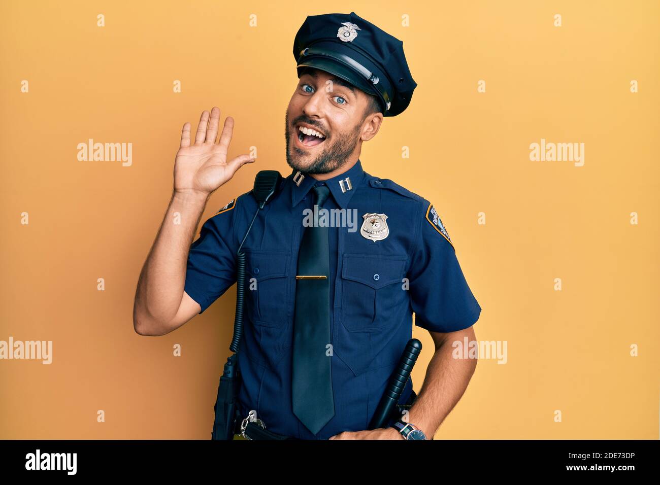 Handsome hispanic man wearing police uniform waiving saying hello happy ...