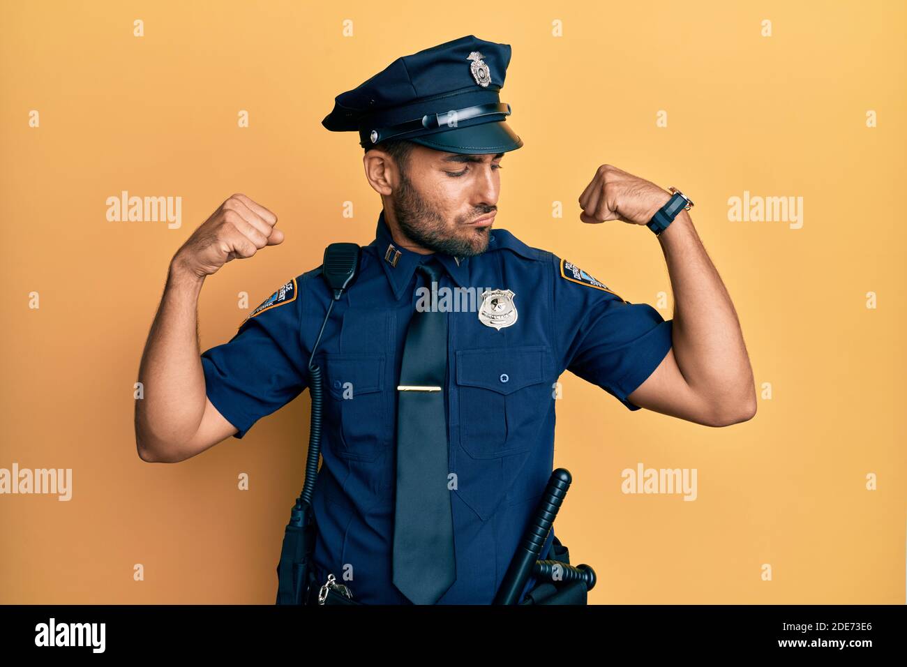 Handsome hispanic man wearing police uniform showing arms muscles ...