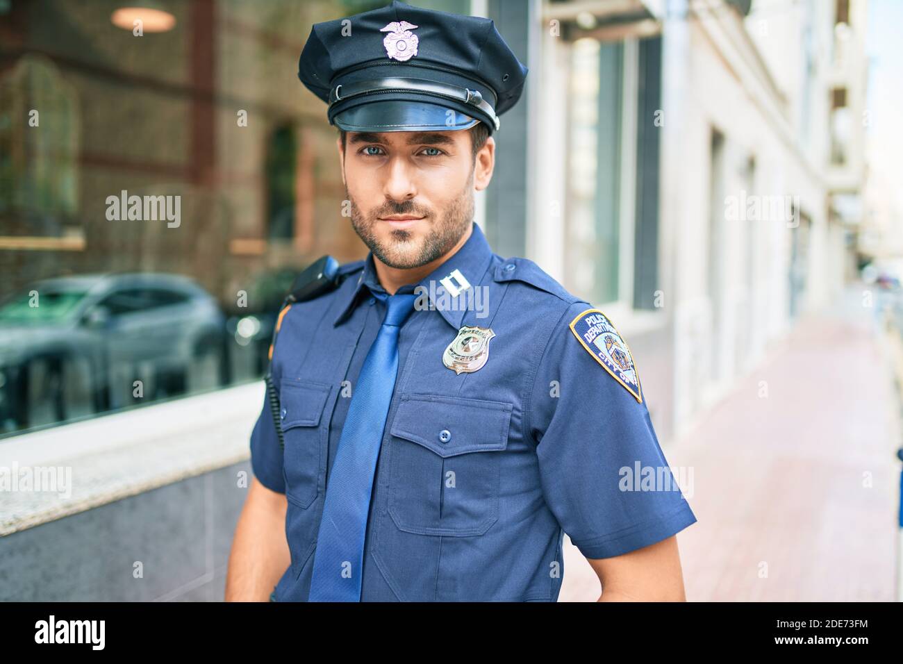 young handsome hispanic policeman wearing police uniform. Standing with ...