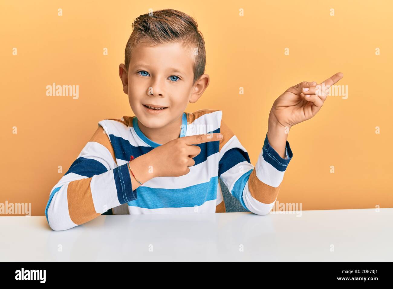 Adorable caucasian kid wearing casual clothes sitting on the table ...