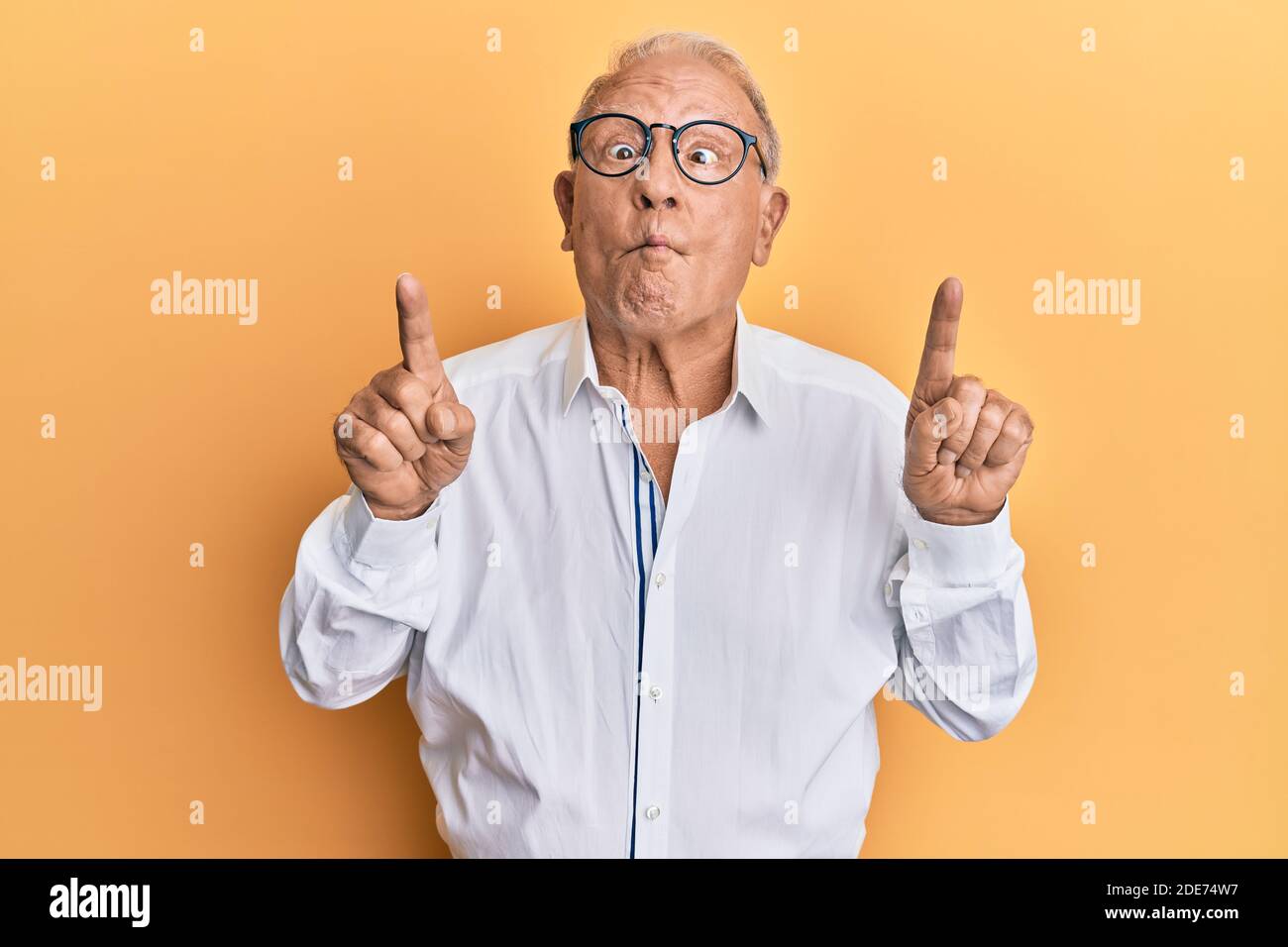 Senior caucasian man pointing up with fingers making fish face with ...