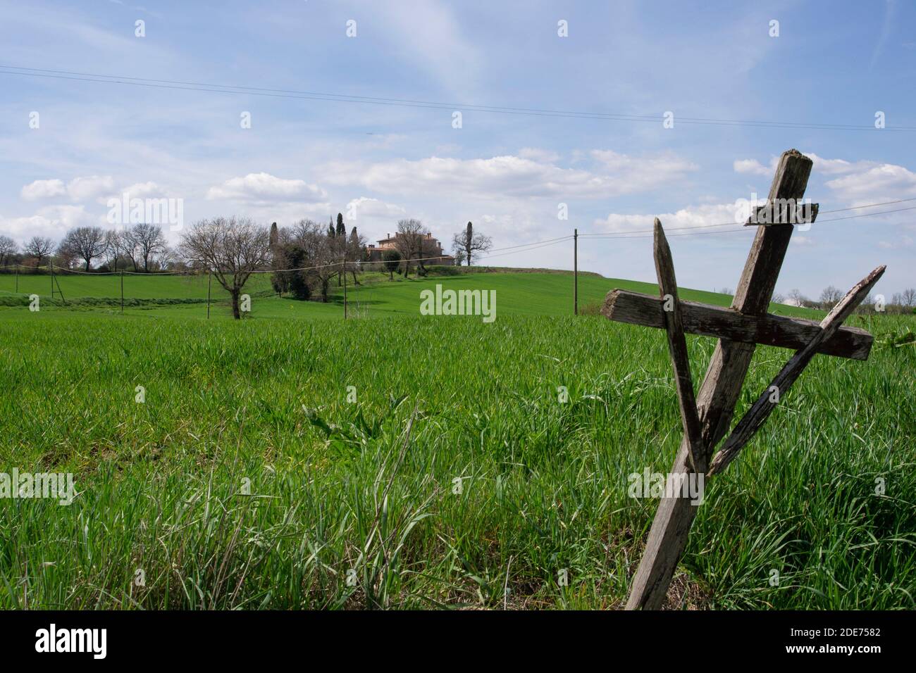 Rolling countryside around a farmhouse. A wooden Christian cross in the ...