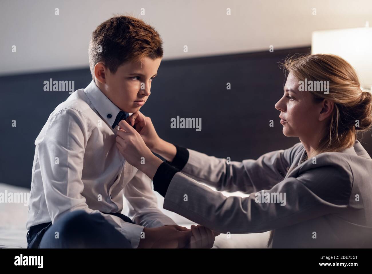 A Mother helping her son to get ready for school, buttoning up his shirt, telling him to behave ...