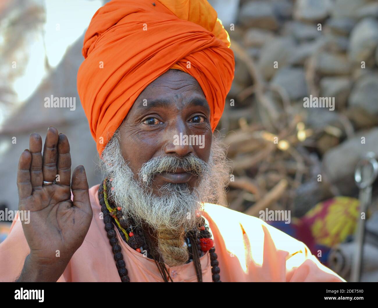 Elderly Indian sadhu with orange turban raises his right hand with the ...