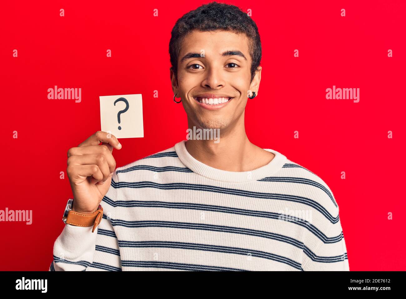 Young african amercian man holding question mark reminder looking ...