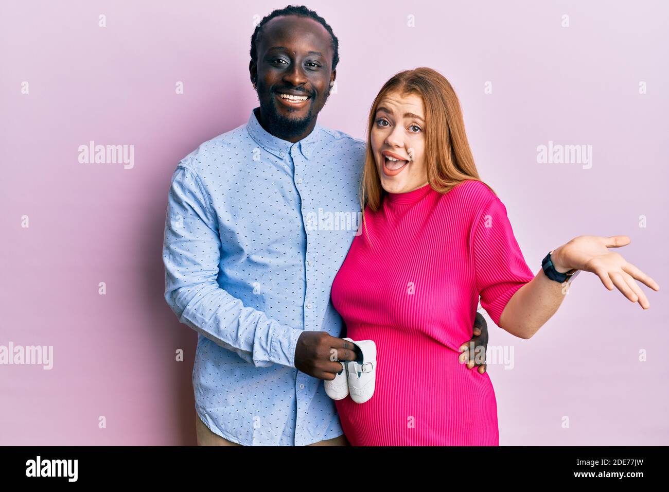 Young interracial couple expecting a baby holding shoes celebrating ...