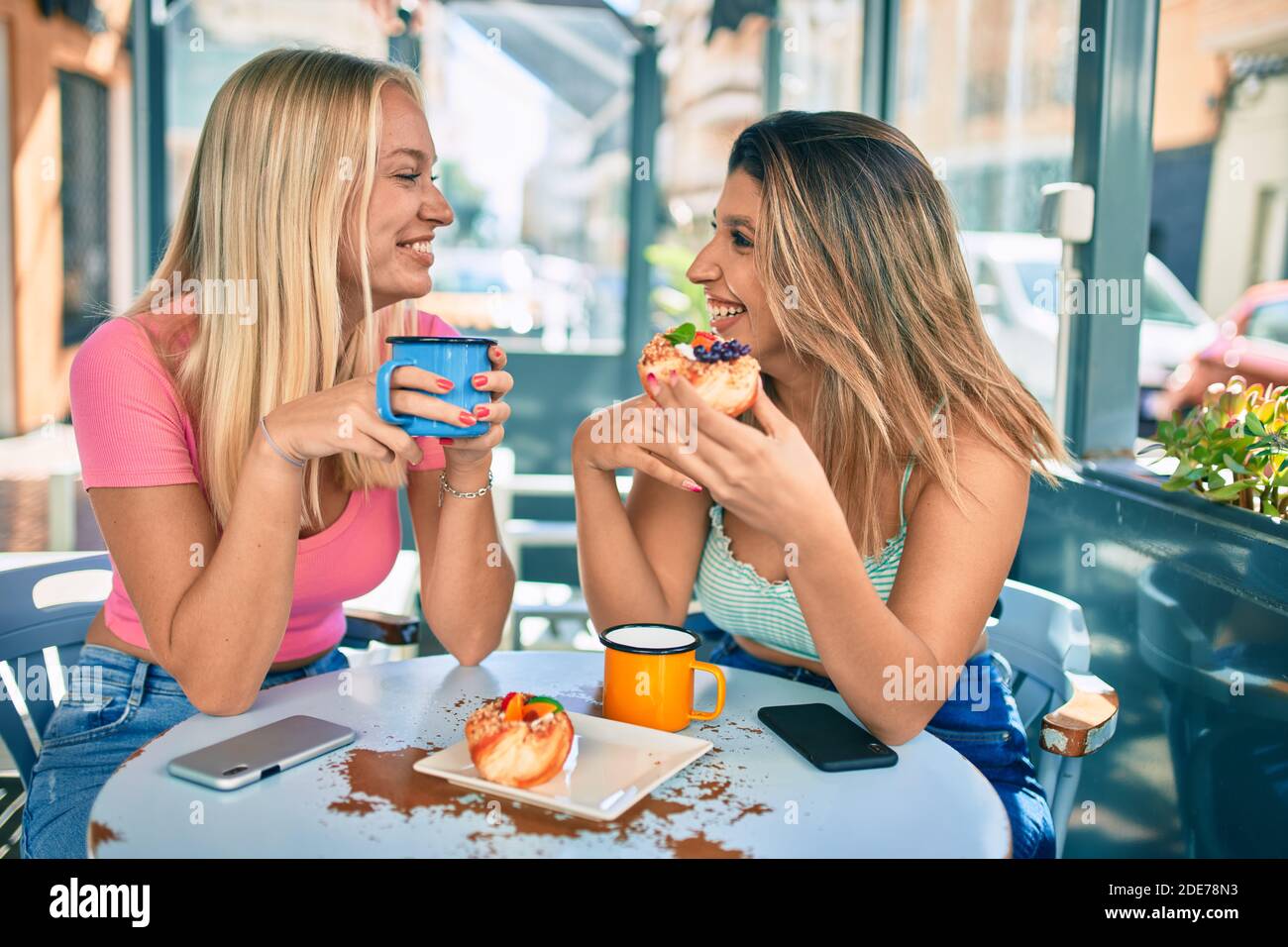 Two beautiful and young girl friends together having fun at cafeteria ...
