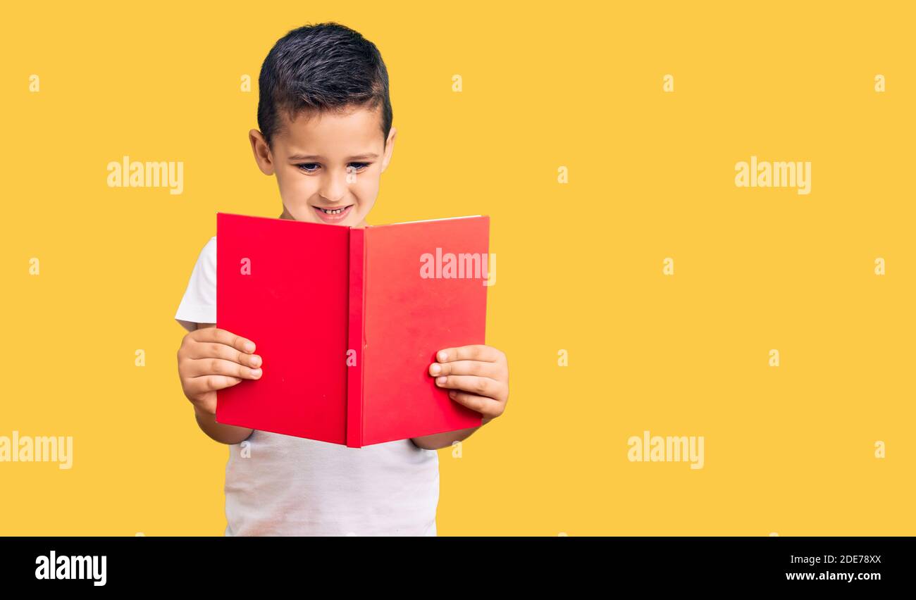 Little cute boy kid reading a book looking positive and happy standing ...