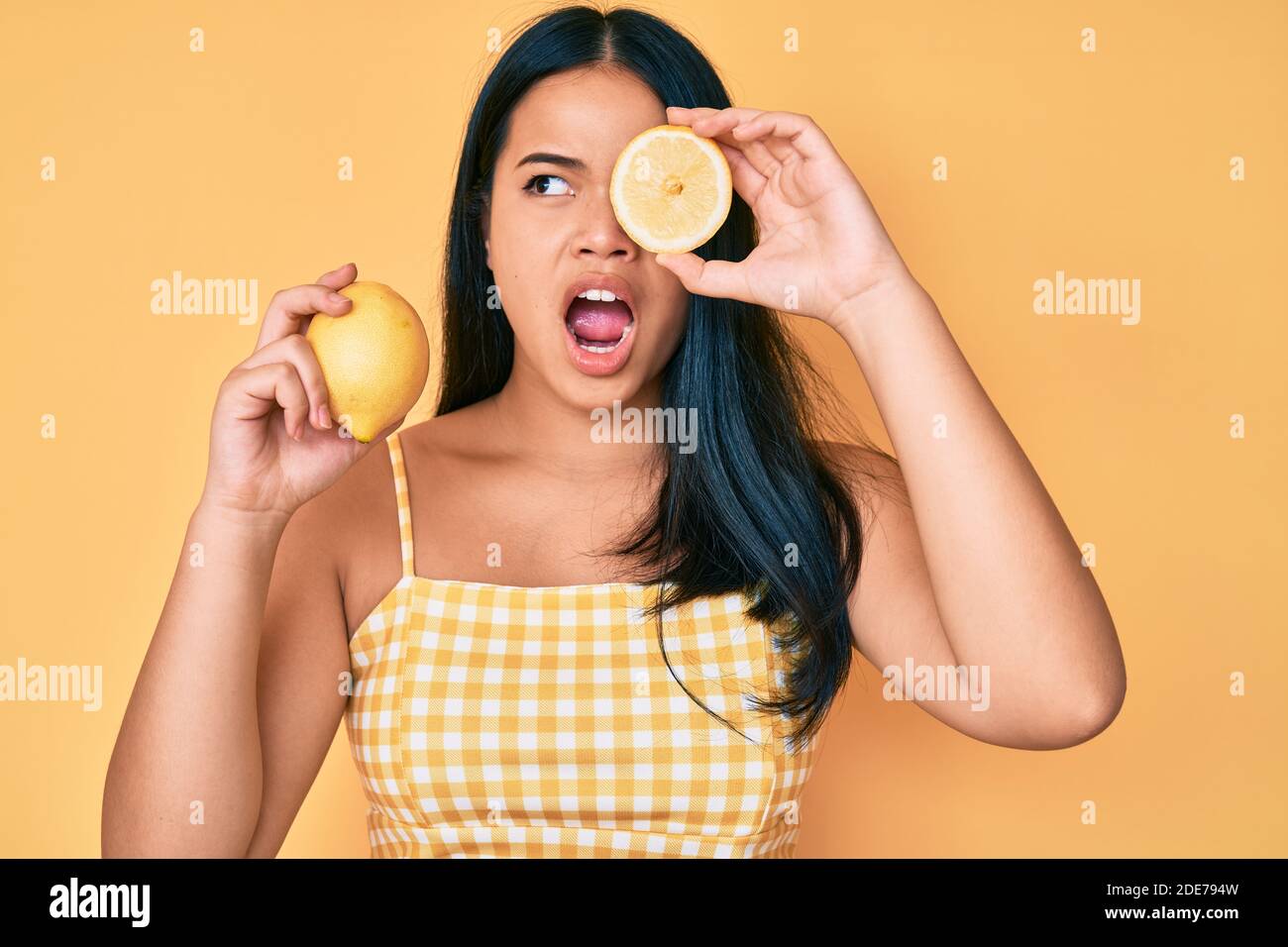 Young beautiful asian girl holding lemon angry and mad screaming ...