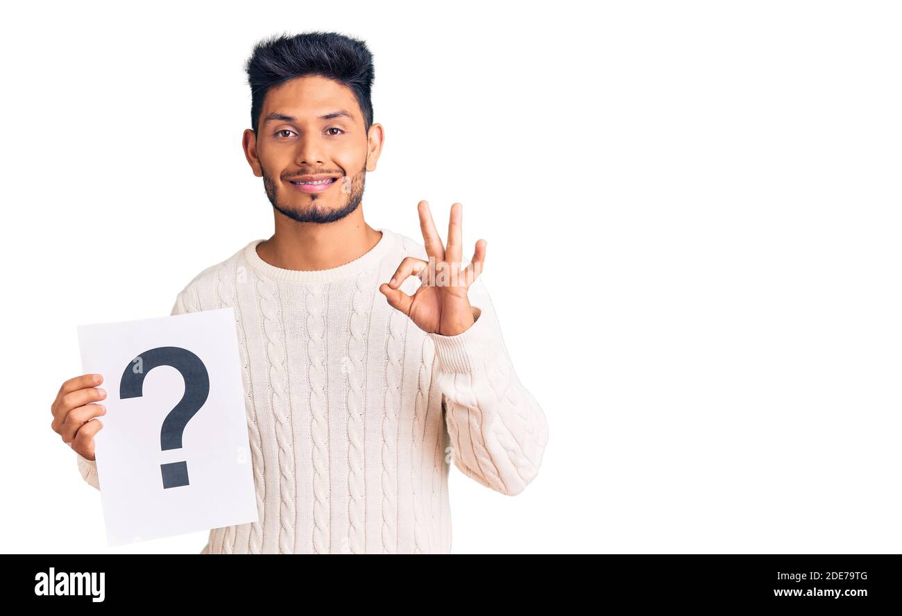 Handsome latin american young man holding question mark doing ok sign ...