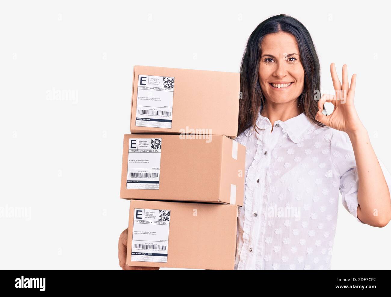 Young beautiful brunette woman holding delivery cardboard package doing ...