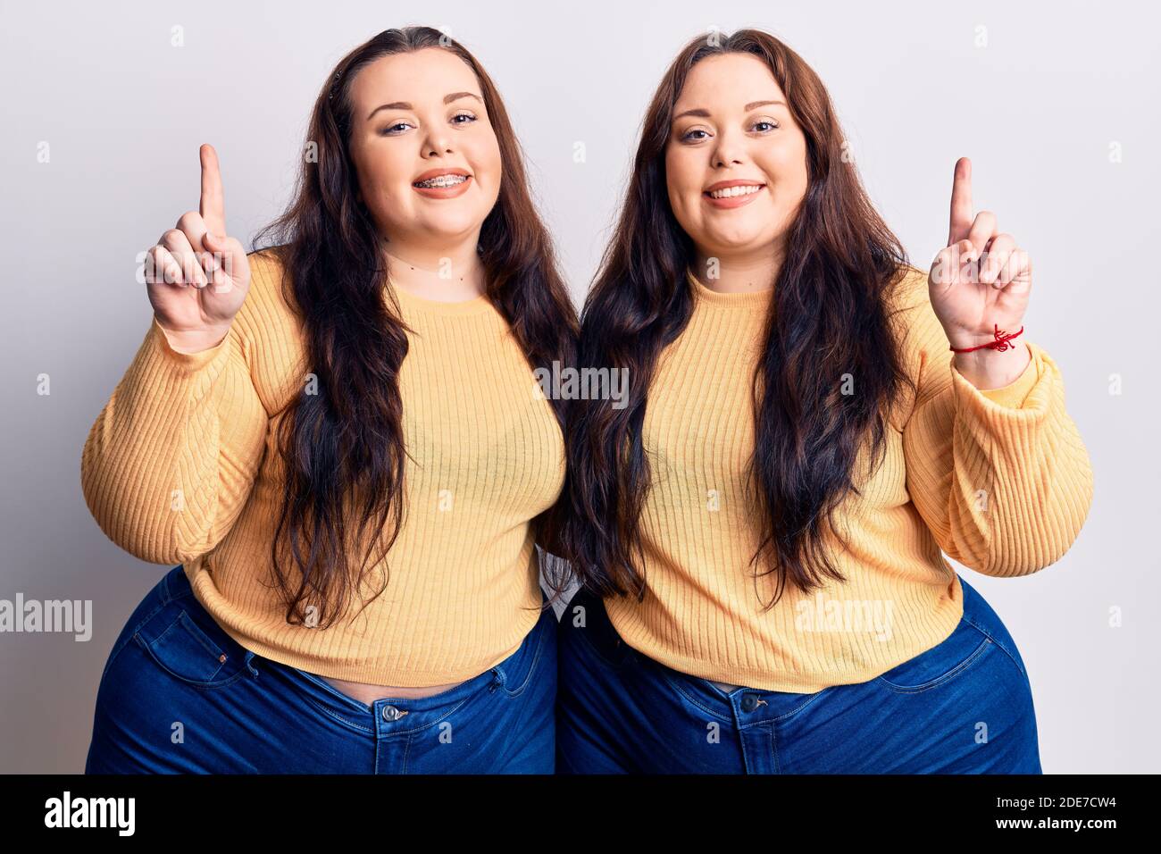 Young plus size twins wearing casual clothes pointing finger up with ...