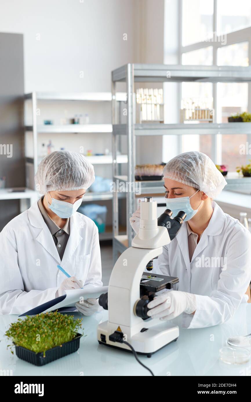 Vertical portrait of two young female scientists looking in microscope ...