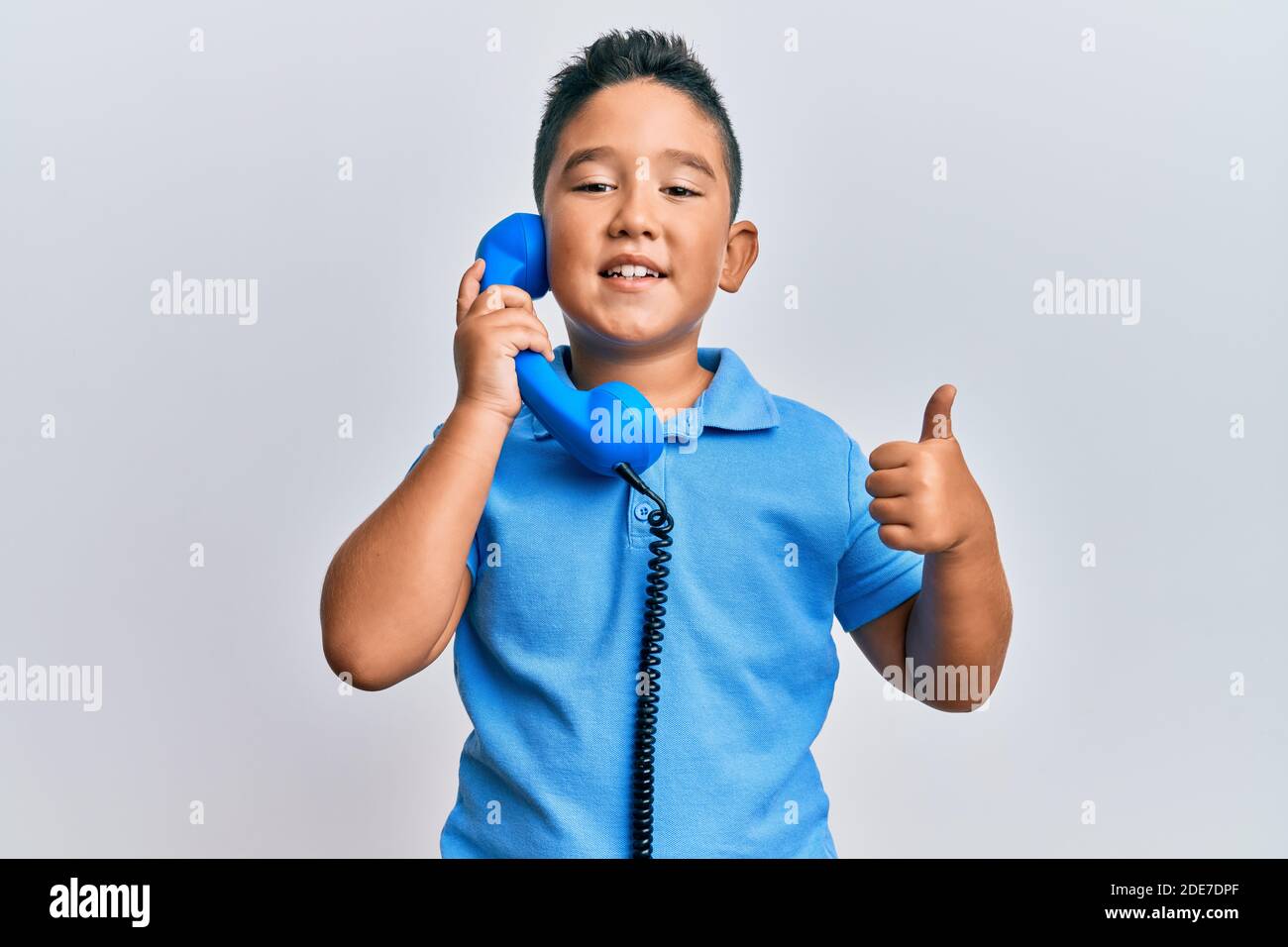Little boy hispanic kid talking through vintage telephone smiling happy ...