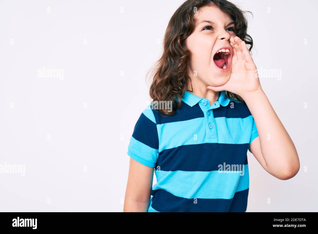 Cute hispanic child with long hair wearing casual clothes shouting and ...