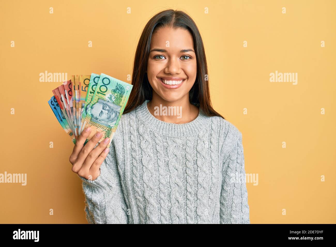 Beautiful hispanic woman holding australian dollars looking positive ...