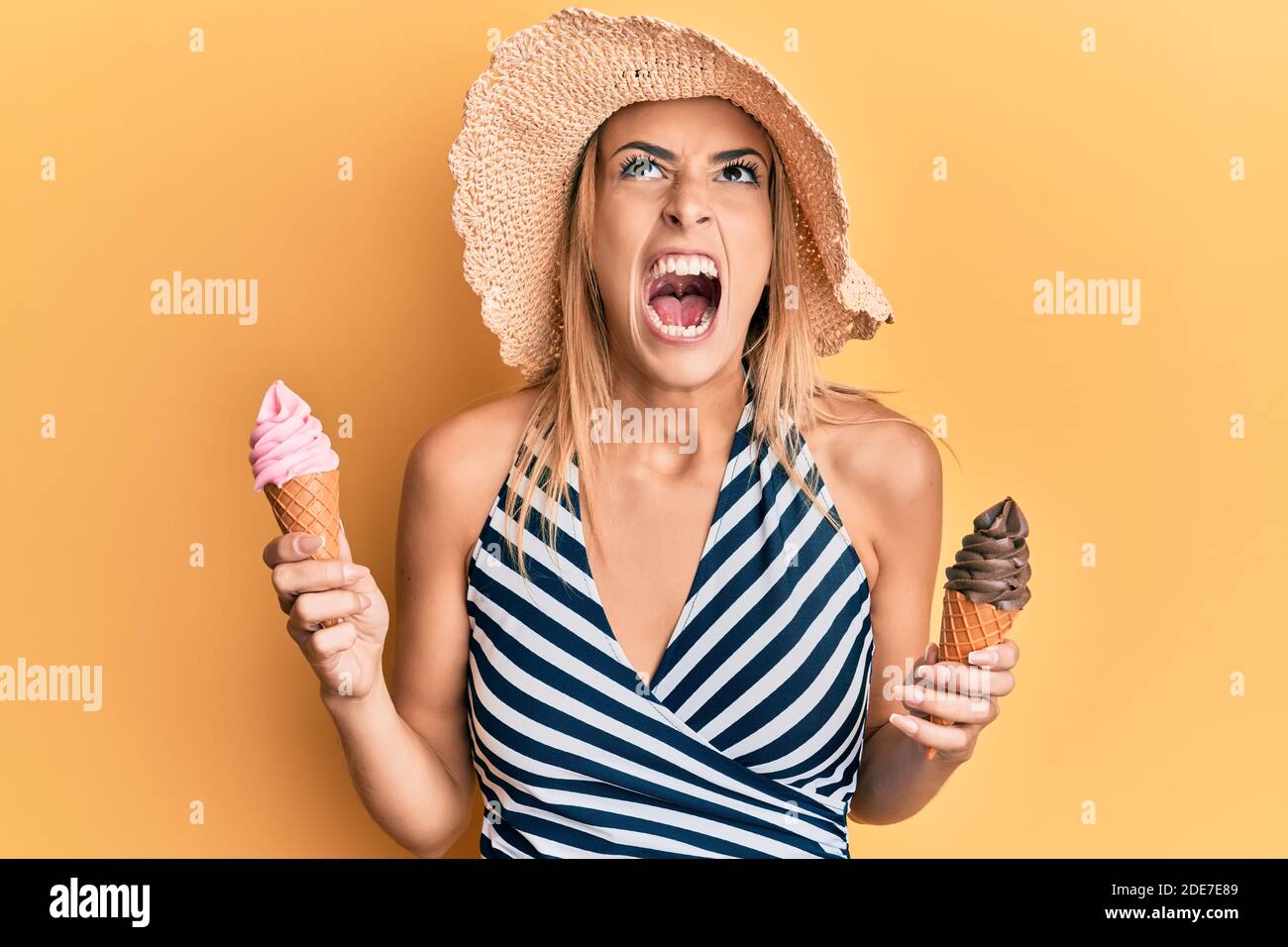 Beautiful blonde woman wearing summer style holding ice cream angry and ...