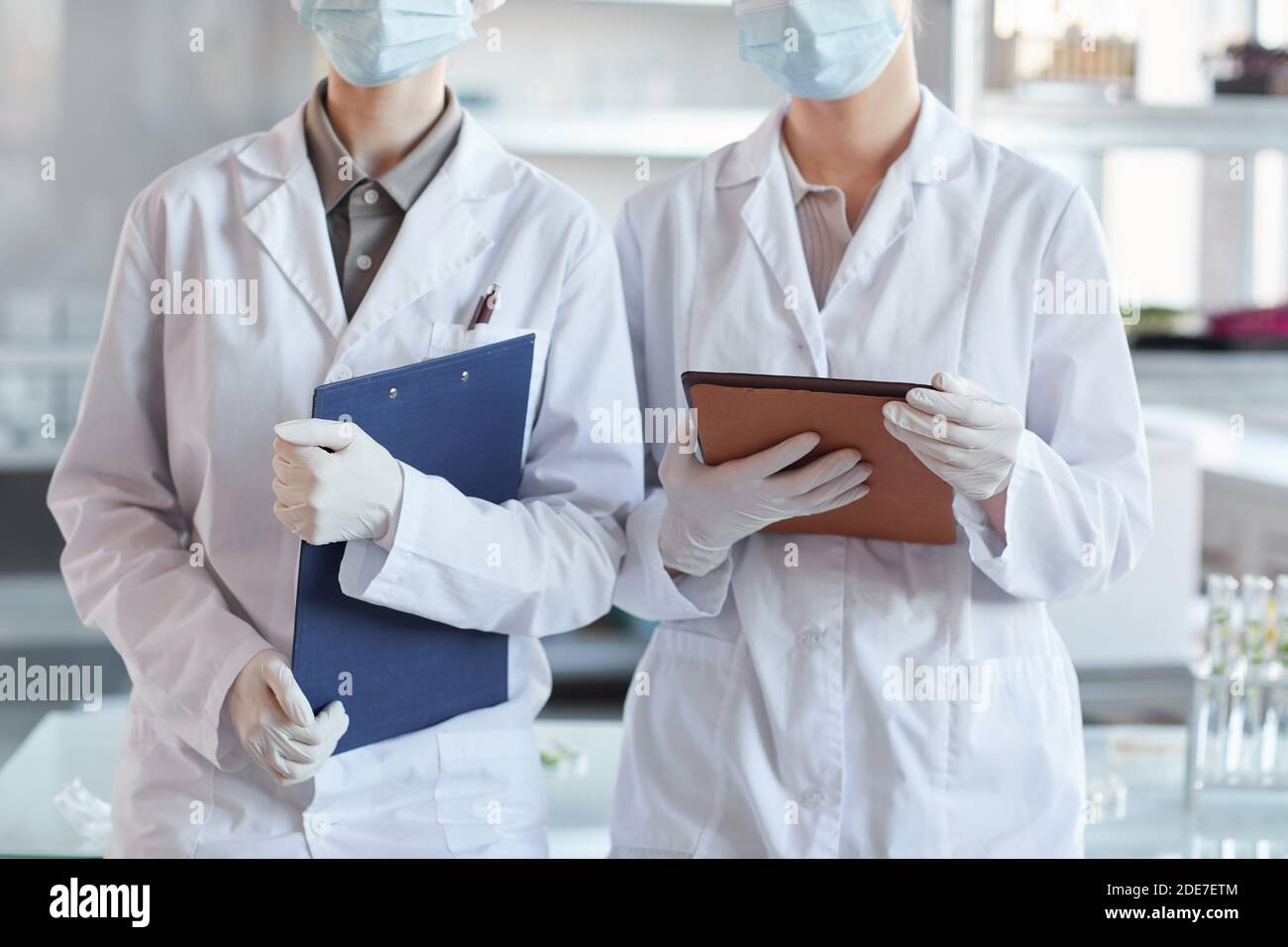 Cropped portrait of two female scientists wearing face mask and holding ...