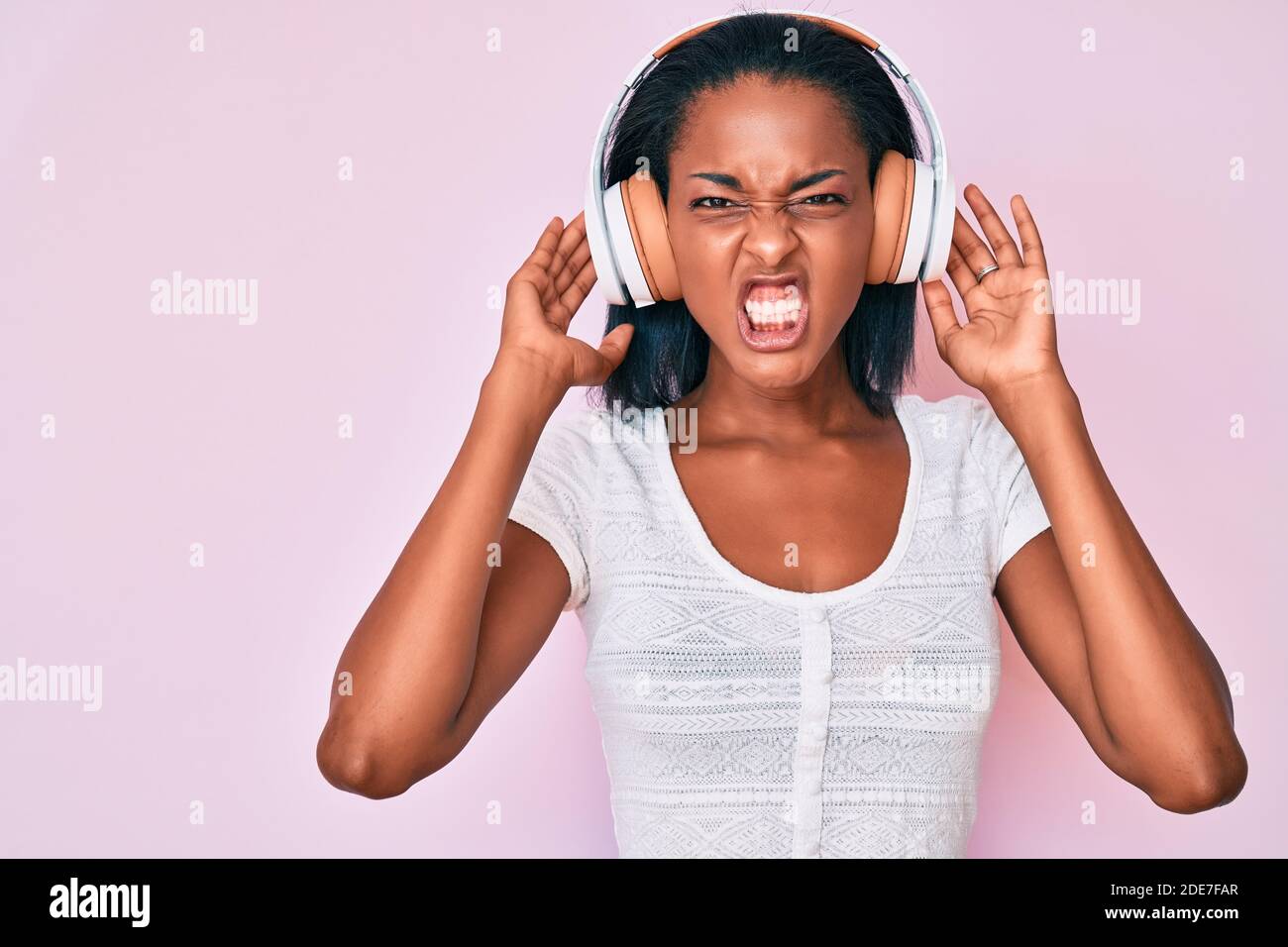 Young african american woman listening to music using headphones angry ...