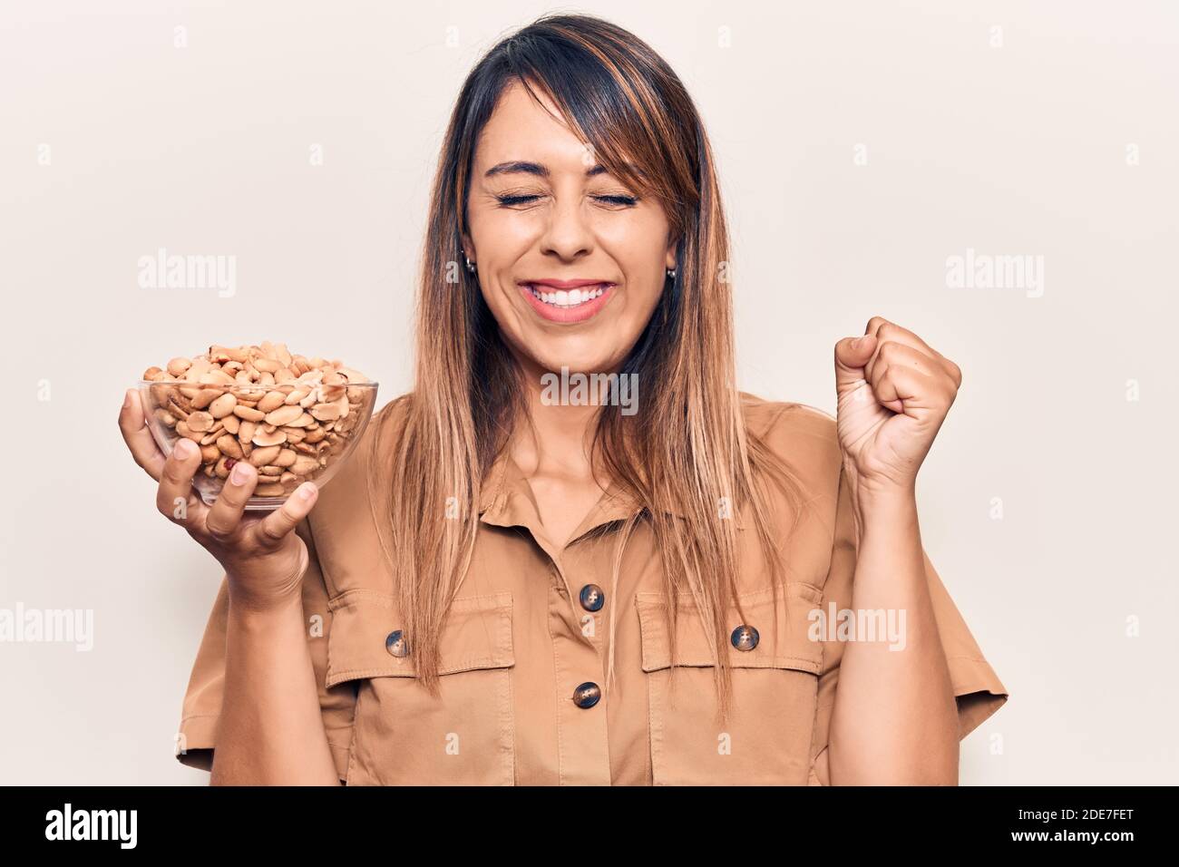Young beautiful woman holding bowl with peanuts screaming proud ...