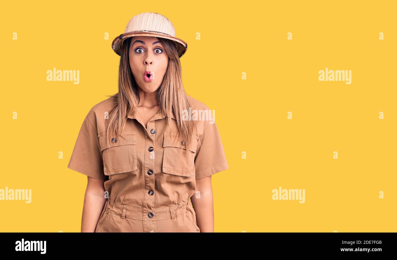 Young beautiful woman wearing explorer hat scared and amazed with open ...