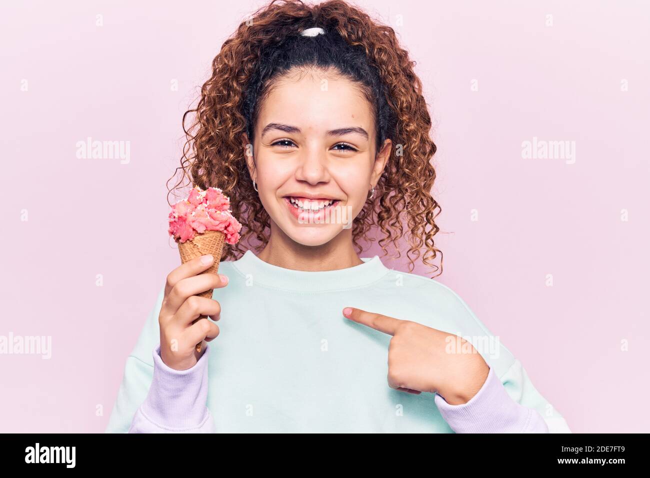 Beautiful kid girl with curly hair holding ice cream pointing finger to ...