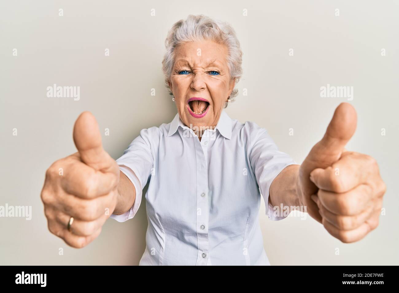 Senior grey-haired woman doing thumbs up positive gesture smiling and ...