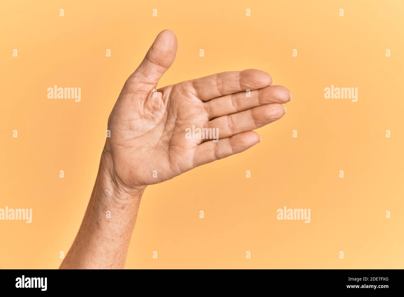 Senior caucasian hand over yellow isolated background presenting with ...