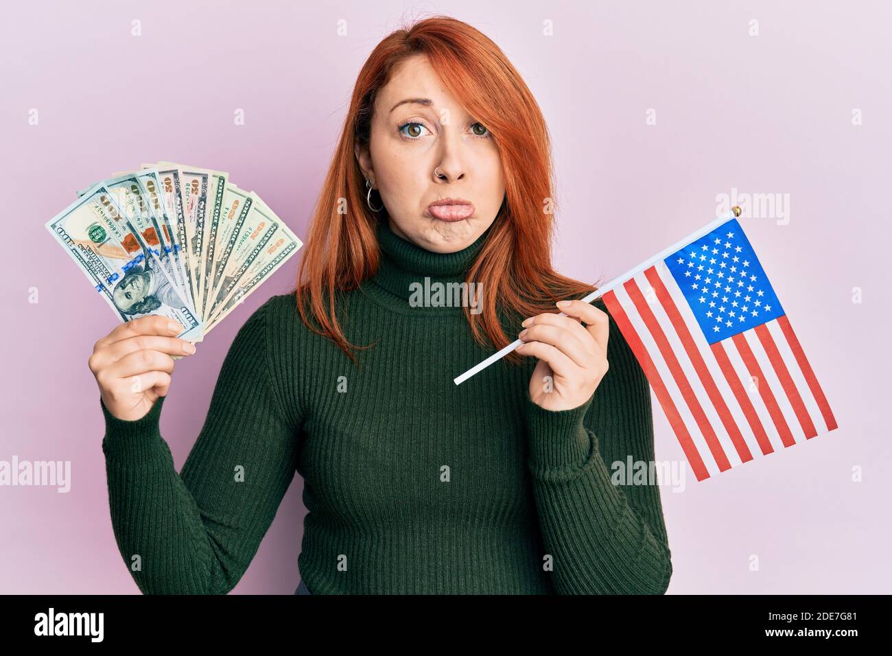 Beautiful redhead woman holding dollars banknote and usa flag depressed ...
