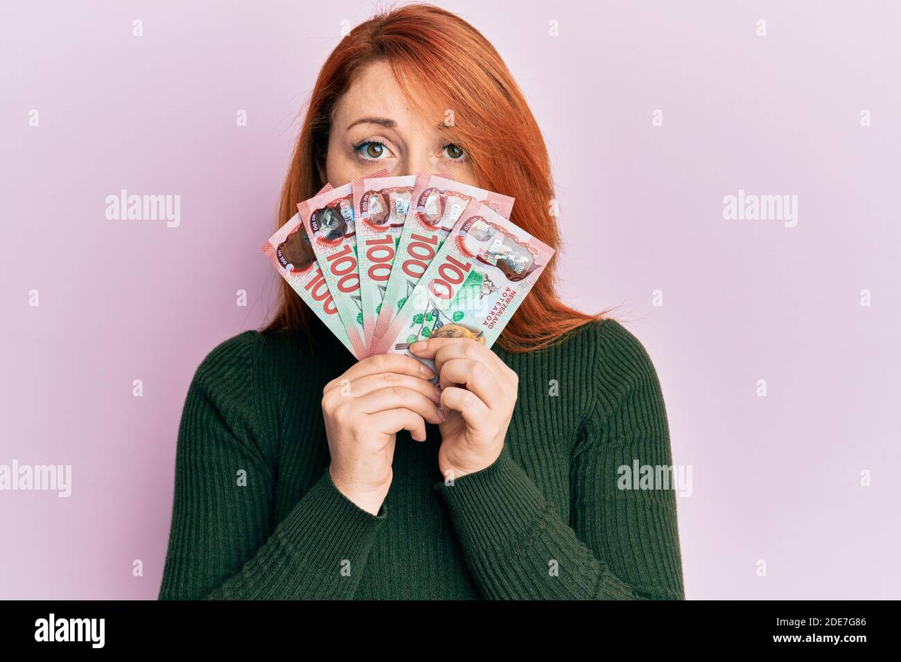 Beautiful redhead woman holding 100 new zealand dollars banknote ...