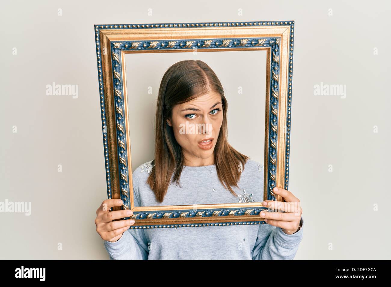 Beautiful caucasian woman holding empty frame in shock face, looking ...