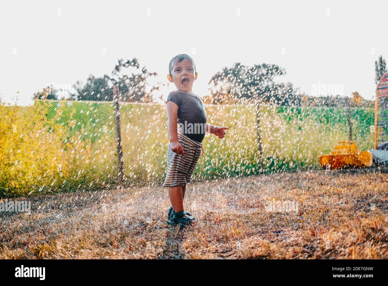 Happy adorable toddler boy having fun under rain. Baby laughs, he is ...