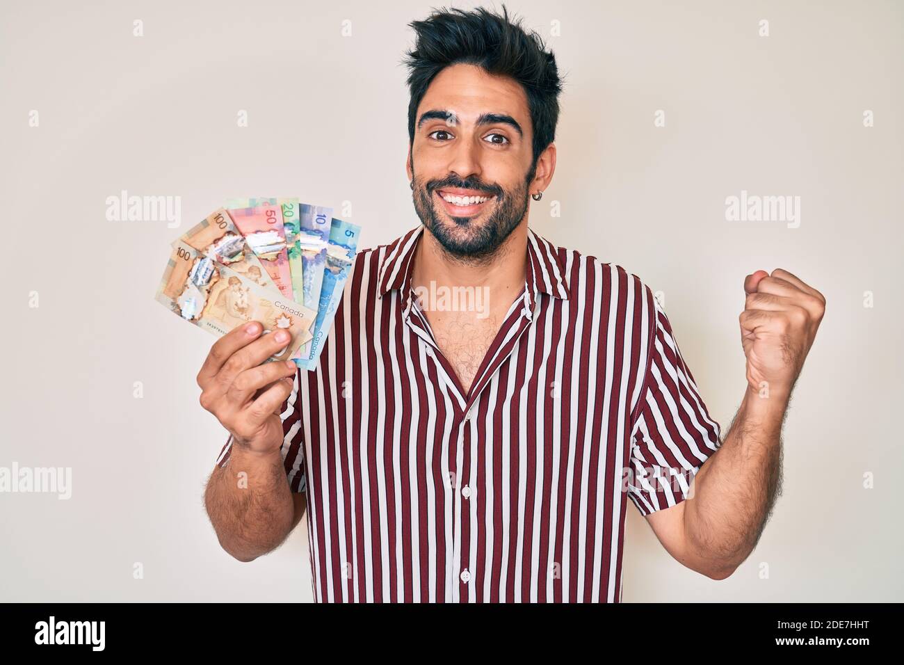 Handsome hispanic man with beard holding canadian dollars screaming ...