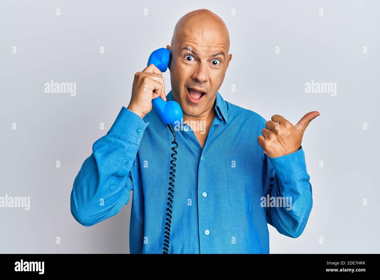 Middle age bald man speaking on vintage telephone pointing thumb up to ...