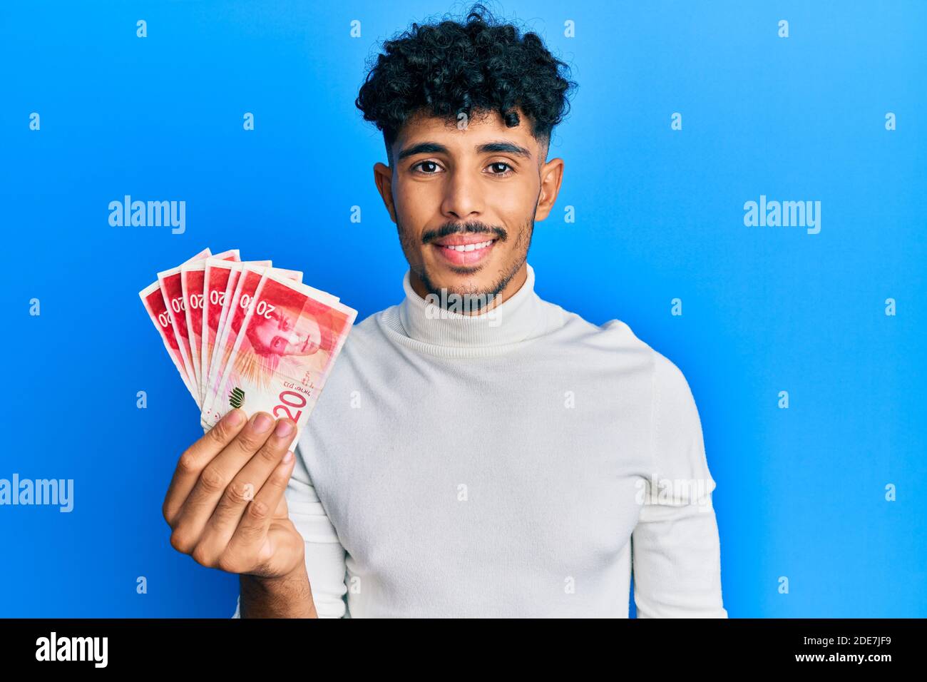 Young arab handsome man holding 20 israel shekels banknotes looking ...