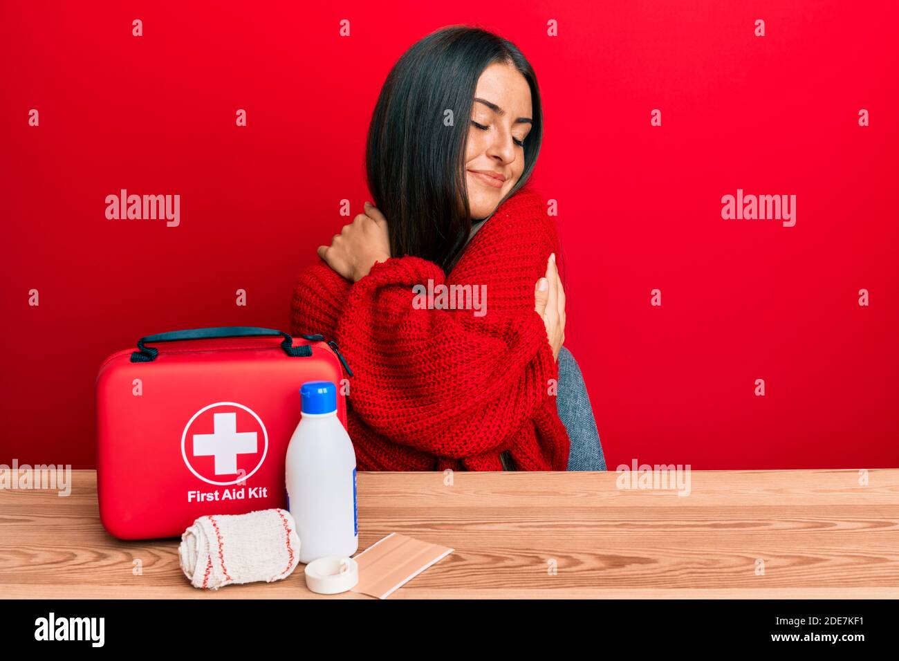 Beautiful hispanic woman with first aid kit hugging oneself happy and ...