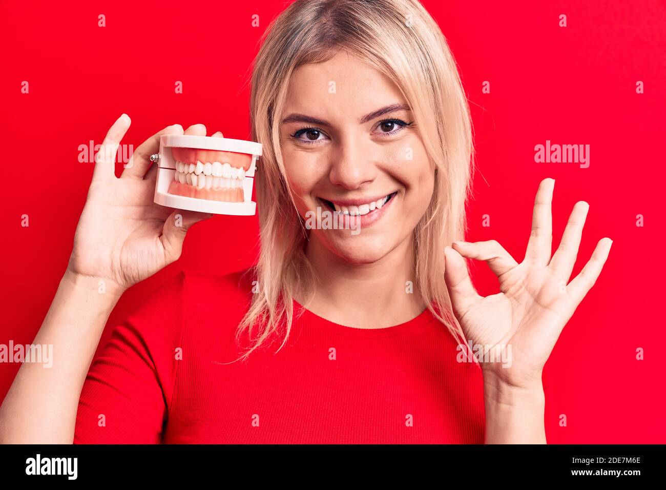 Young beautiful blonde woman holding denture teeth standing over ...