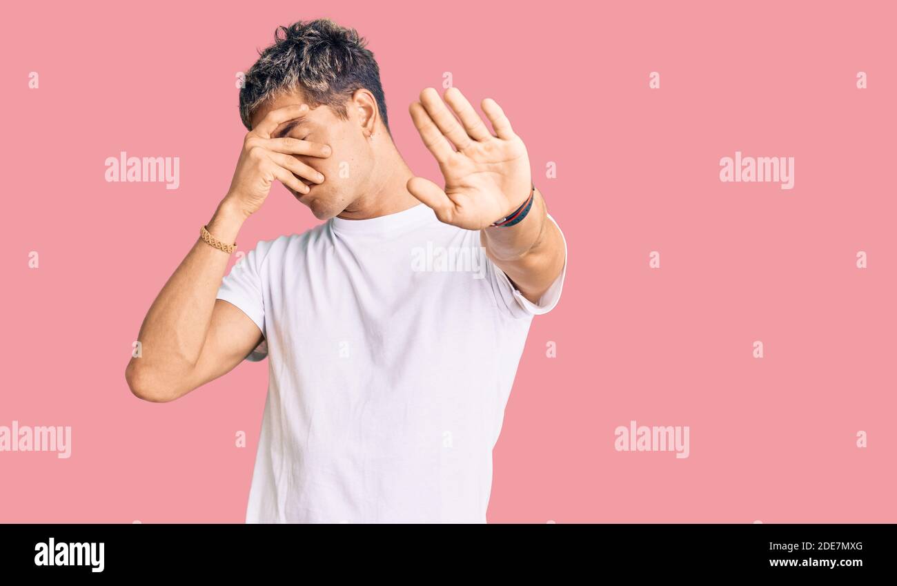 Young handsome man wearing casual white tshirt covering eyes with hands ...