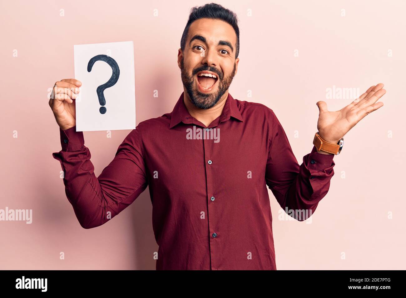 Young hispanic man holding question mark celebrating achievement with ...