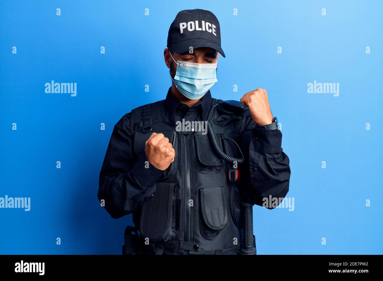 Young hispanic man wearing police uniform and medical mask celebrating ...