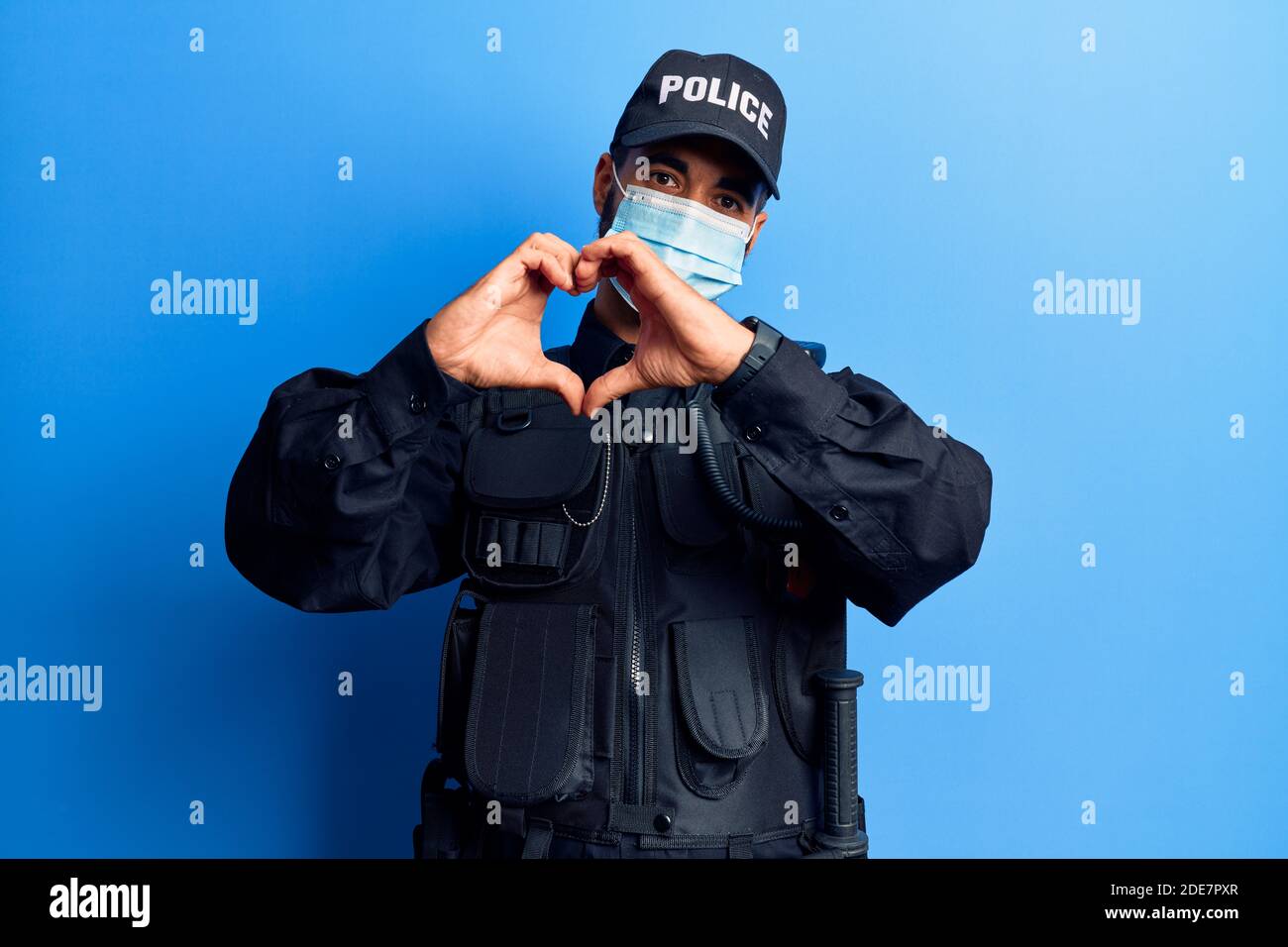 Young hispanic man wearing police uniform and medical mask smiling in ...