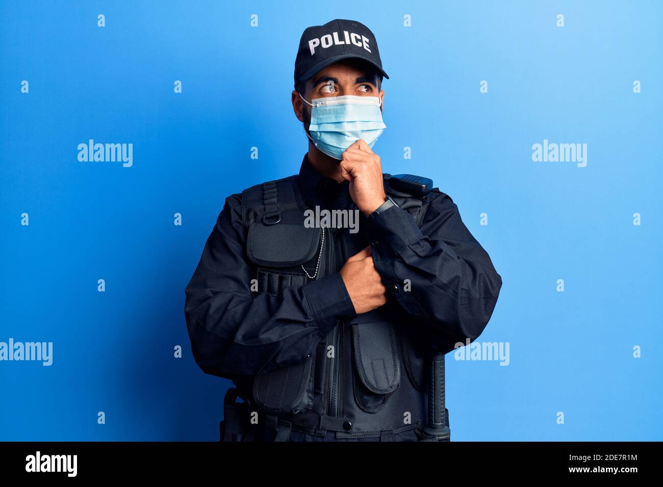 Young hispanic man wearing police uniform and medical mask thinking ...