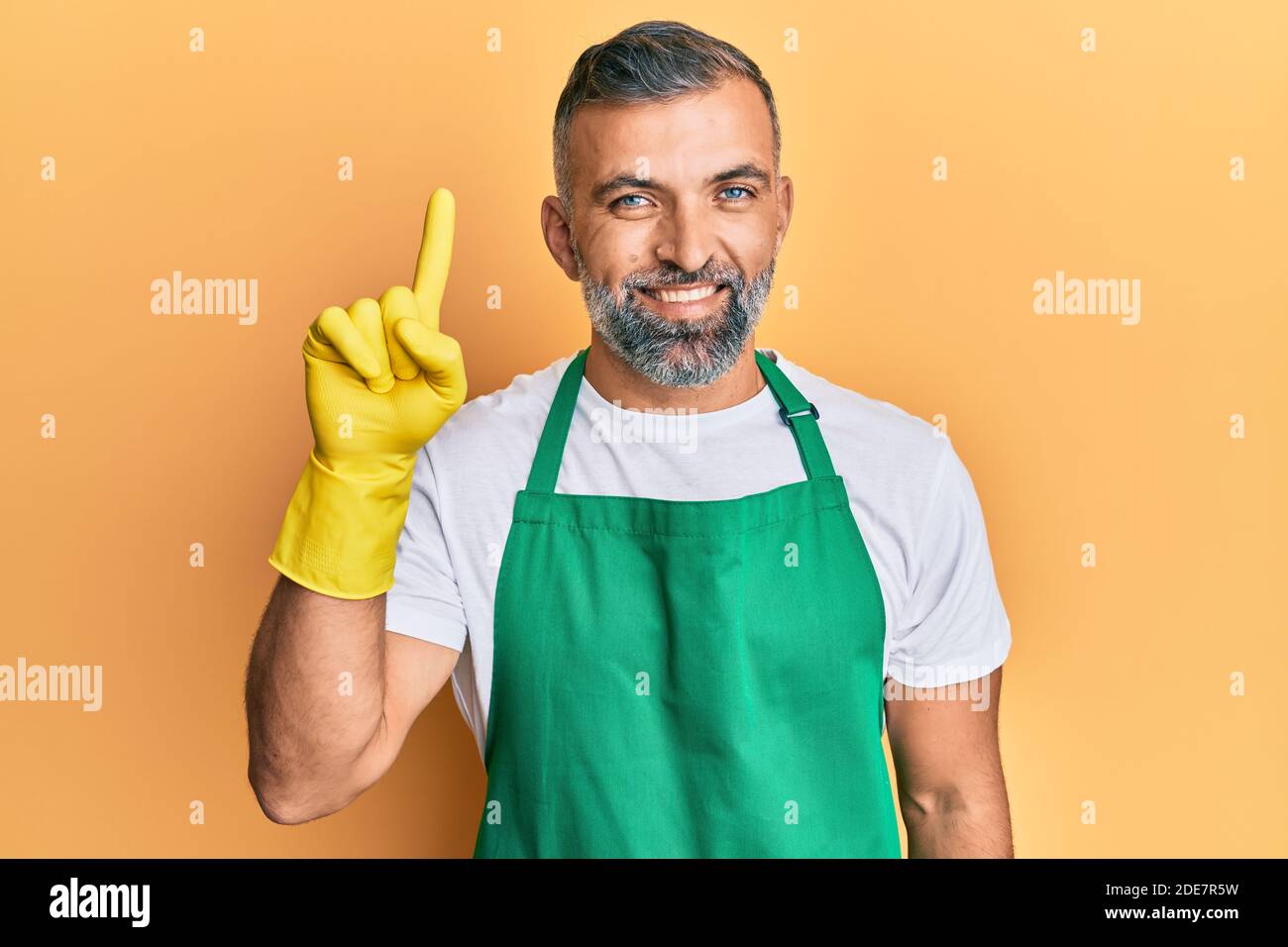 Middle age handsome man wearing cleaner apron and gloves smiling with ...
