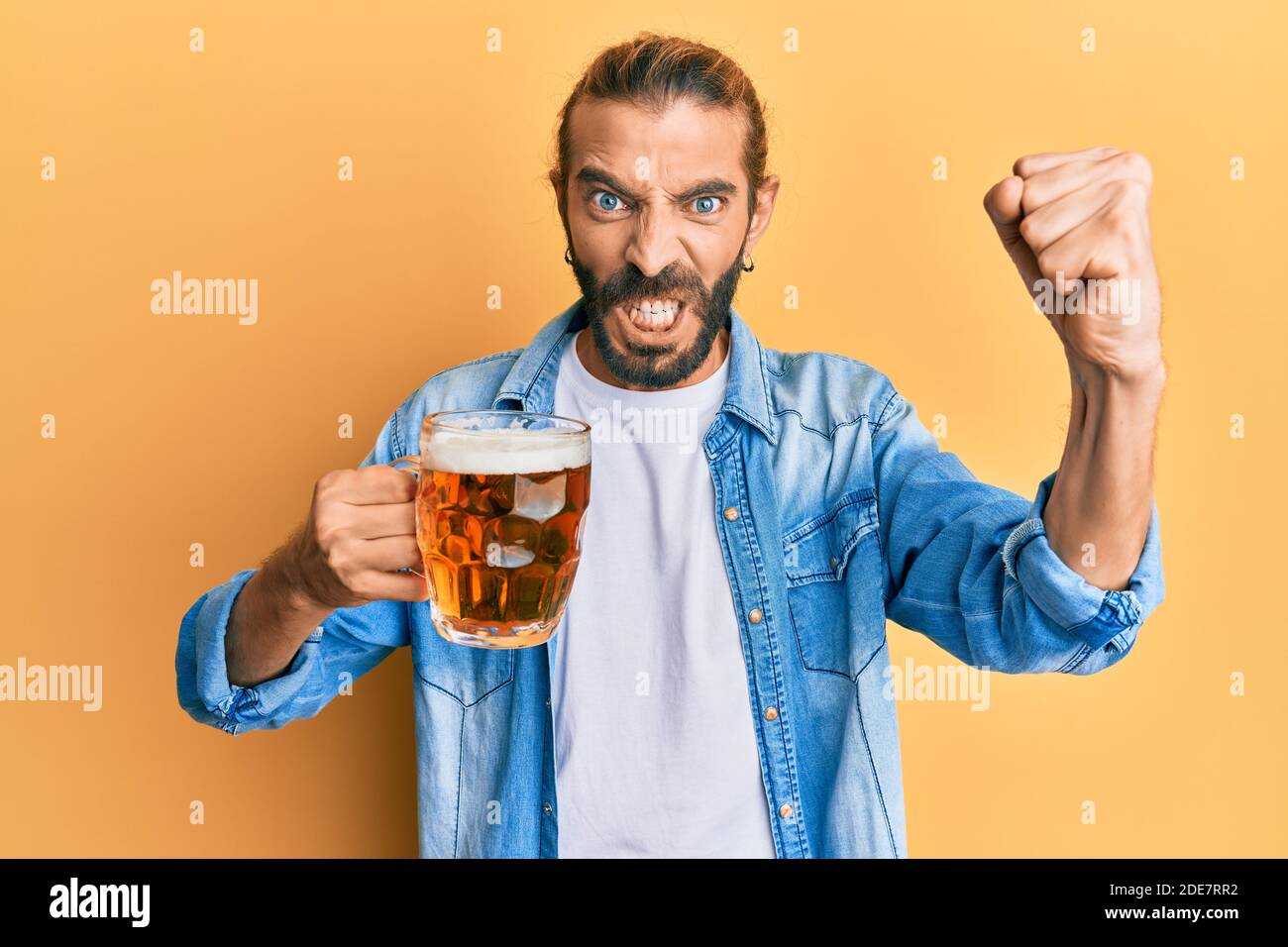 Attractive man with long hair and beard drinking a pint of beer annoyed ...
