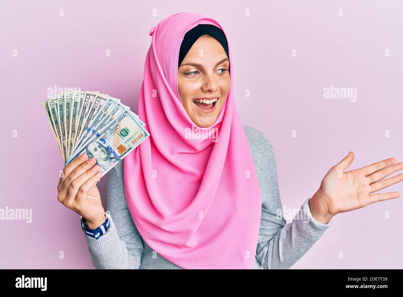 Young caucasian woman wearing islamic hijab holding dollars banknotes ...