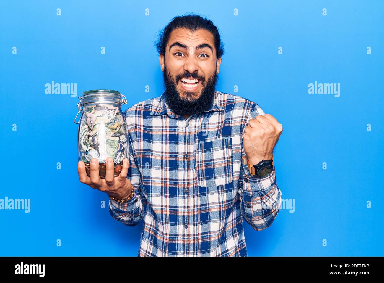 Young arab man holding jar with savings screaming proud, celebrating ...