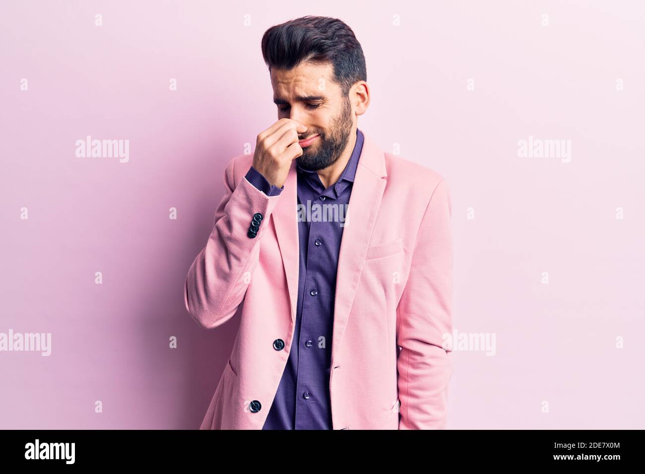 Young handsome man with beard wearing elegant jacket smelling something ...