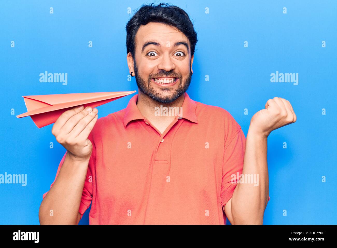 Young hispanic man holding paper airplane screaming proud, celebrating ...