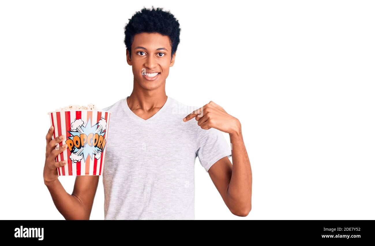 Young african american man holding popcorn pointing finger to one self smiling happy and proud ...