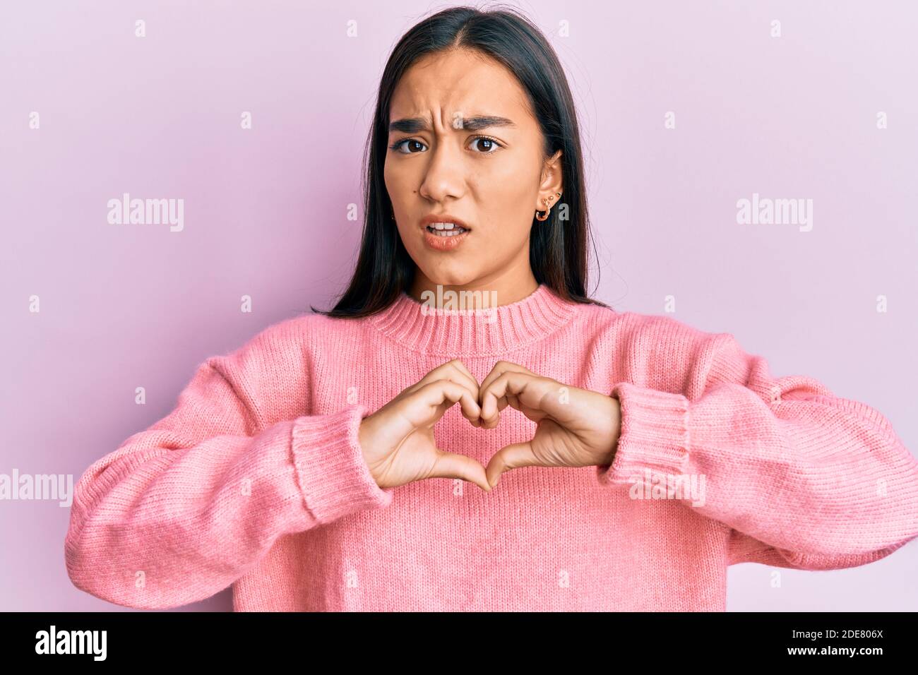 Young asian woman doing heart symbol with hands clueless and confused ...